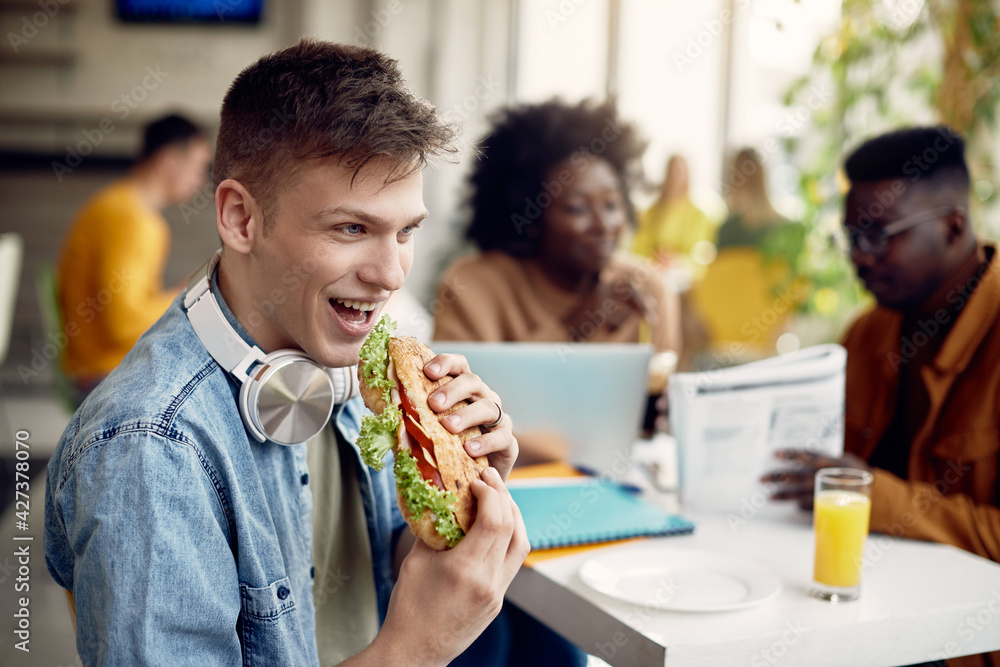 Happy student eating sandwich on lunch break in cafeteria. Stock Photo ...