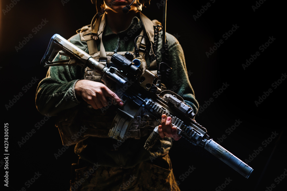 Unrecognizable special forces soldier standing with rifle against black ...