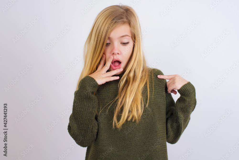 Shocked Caucasian kid girl wearing green knitted sweater against white ...