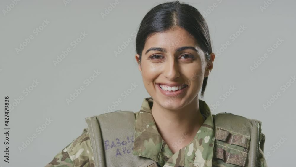 Smiling young female soldier in uniform wearing body armour in front of ...