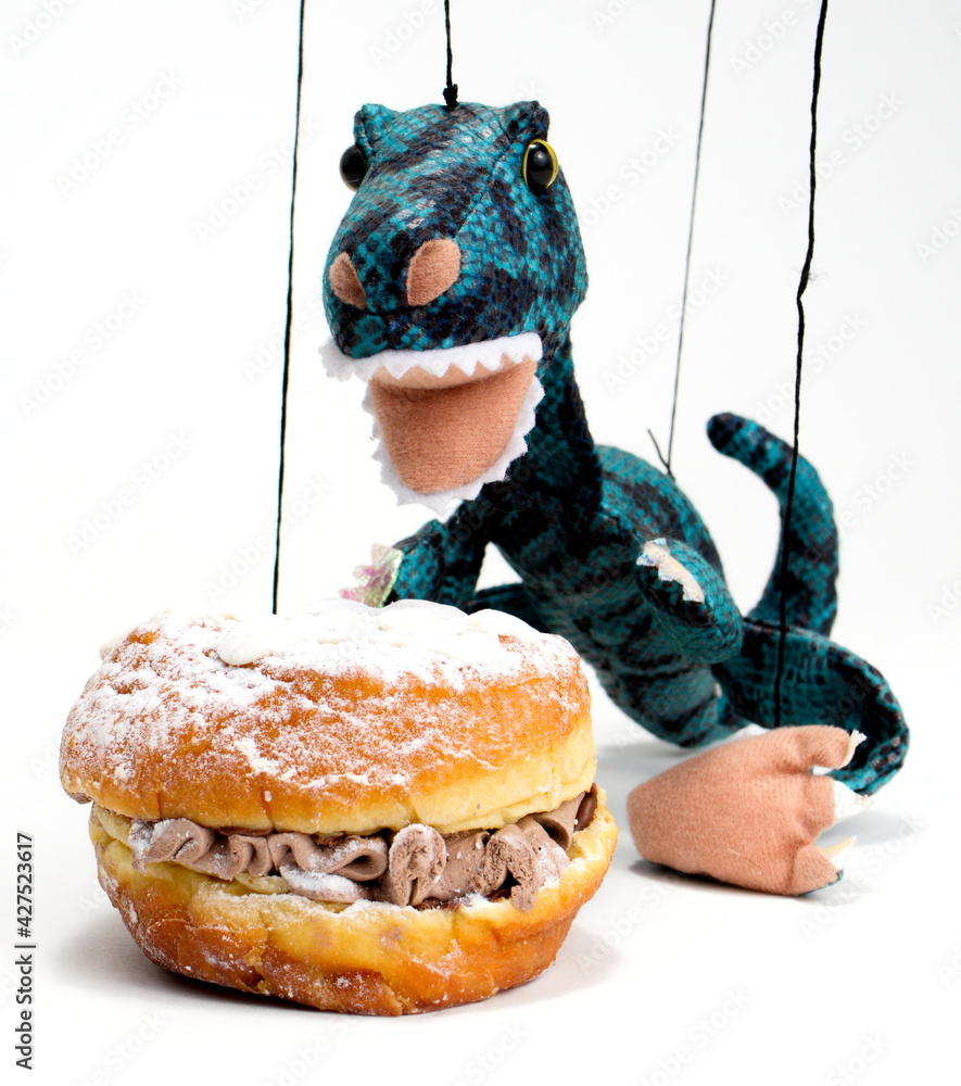 A puppet T-Rex dinosaur sitting down to eat a tasty, cream filled donut ...