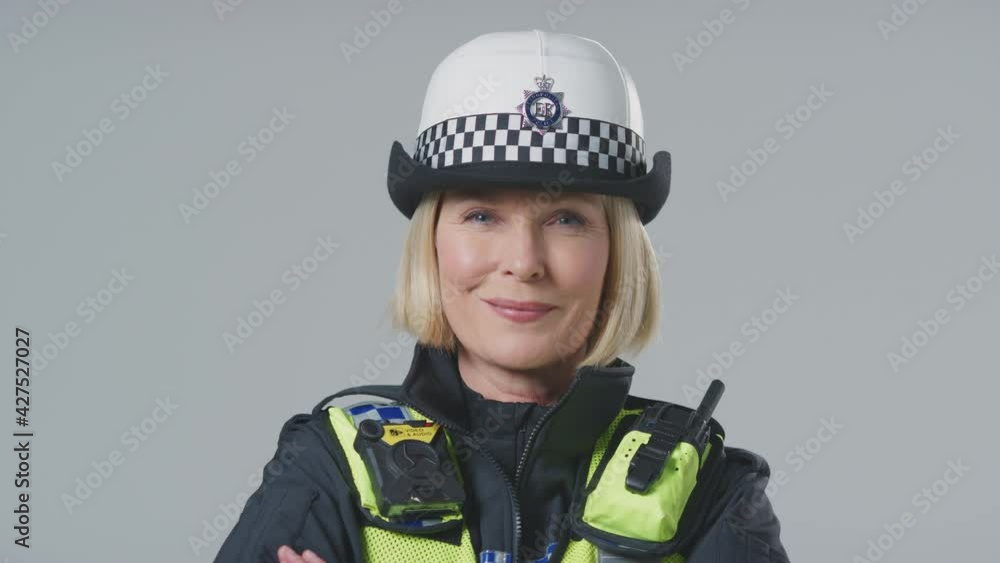 Smiling mature female police office wearing uniform in front of plain ...