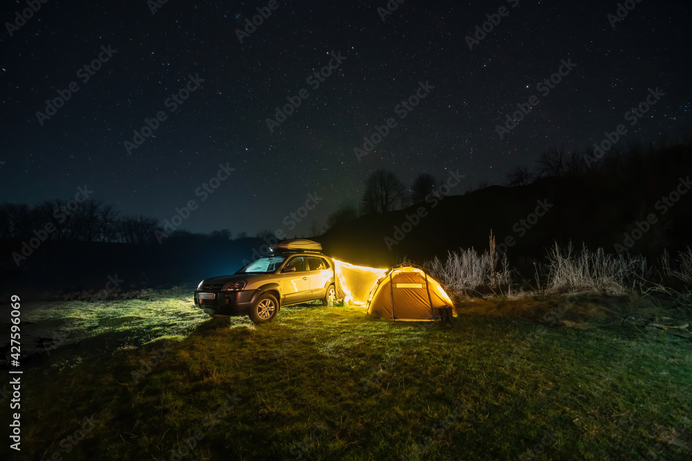 Night landscape with illuminated tent and 4wd car, lights and stars in ...