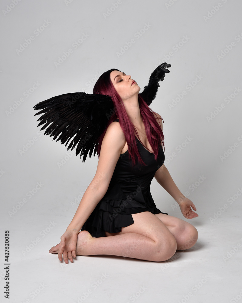 Full Length Portrait Of A Red Haired Girl Wearing Black Dress And Feather Angel Wings Sitting