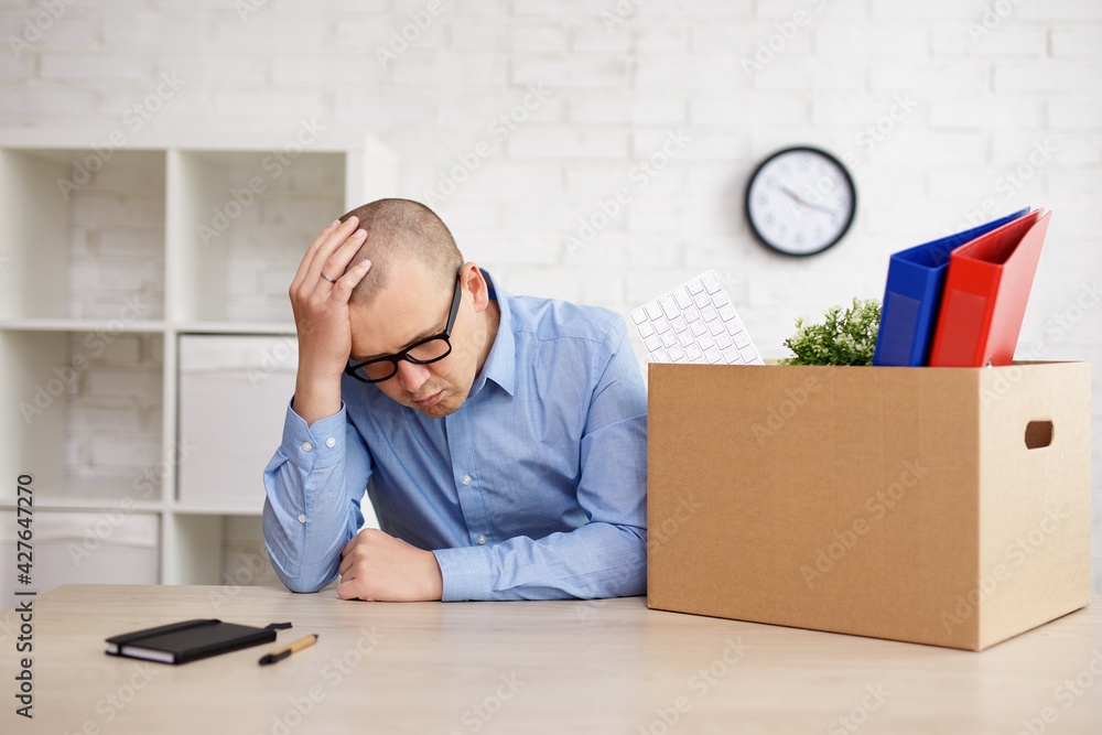 sad businessman sitting in office with moving boxes, covering face with ...