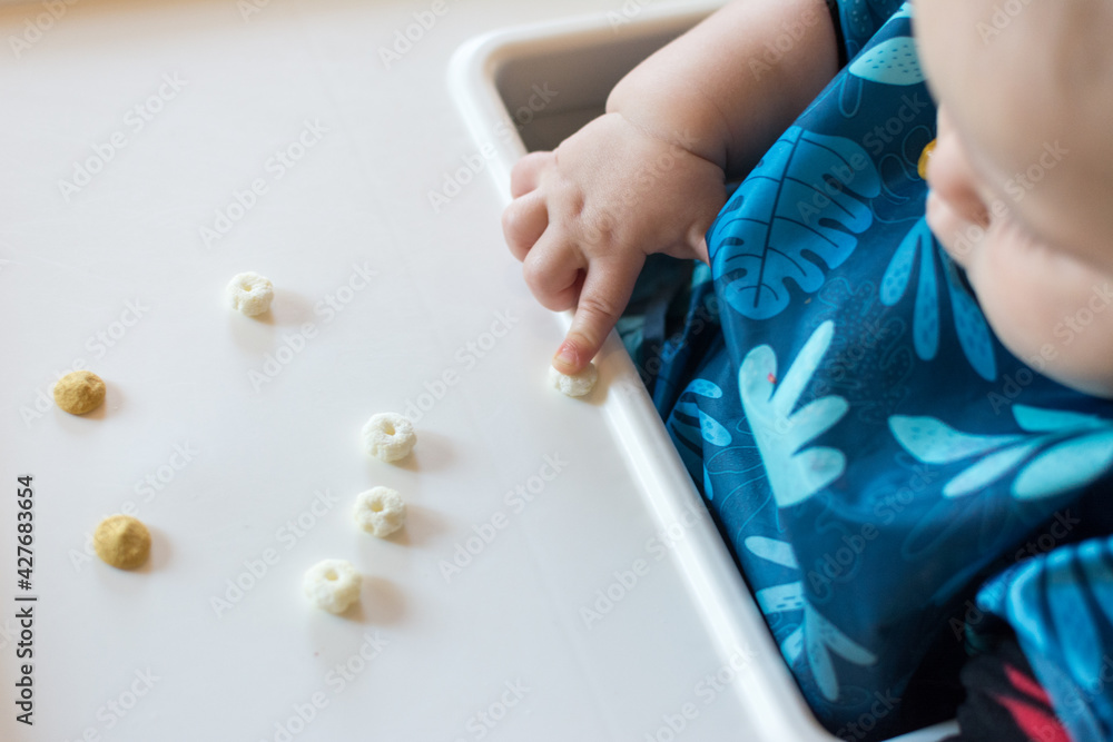 Foto de Baby using pointer finger to drag a cereal puff to edge of tray ...