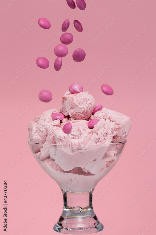 Pink ice cream in a cup with pink candies falling on it, shot in studio ...