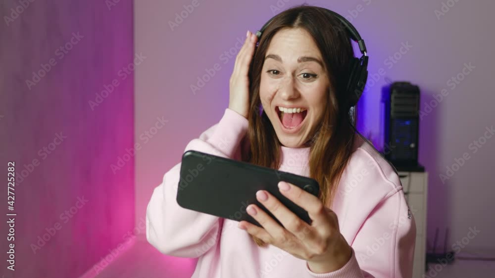 Woman play game with smart phone at neon background. Excited girl ...