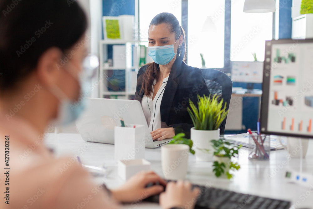 Woman in business new normal office working on laptop behind shiled ...