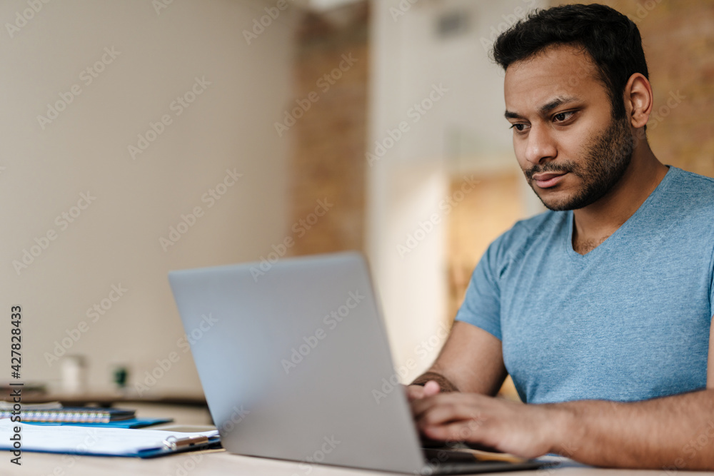 Middle eastern unshaven man working with laptop while sitting at desk ...