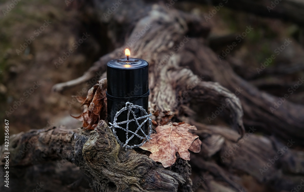 Magic pentagram amulet and black candle in forest. Black magic esoteric ...