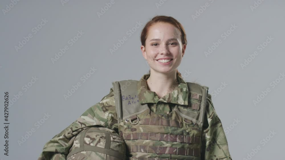 Smiling young female soldier in uniform wearing body armour and holding ...