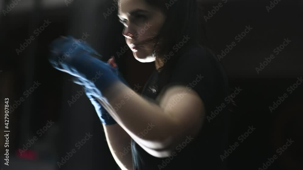 young female boxer wraps bandages around her arms and hits a punching ...