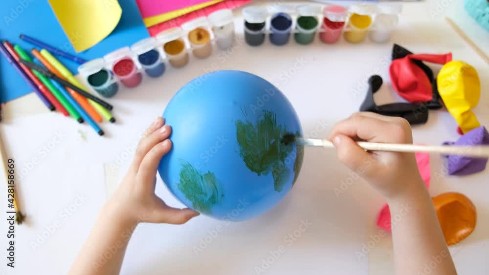Child making planet for earth day from balloon. drawing blue ball with ...