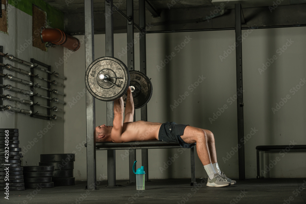 Athletic muscular bodybuilder doing bench press workout indoors in a ...
