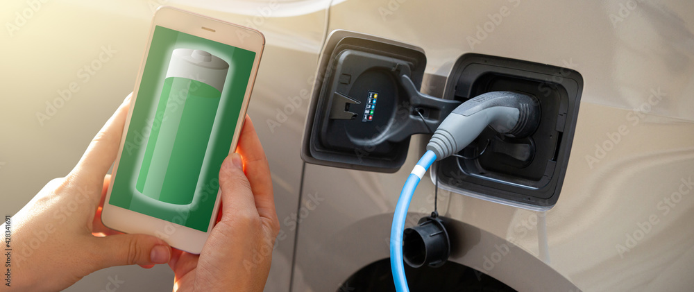 Hands with smartphone on a background of a car at the charging station ...