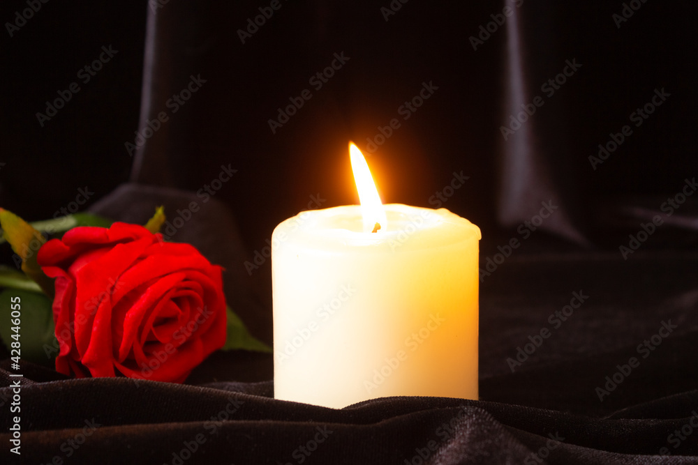 A burning candle and a red rose on a black background. The concept of ...
