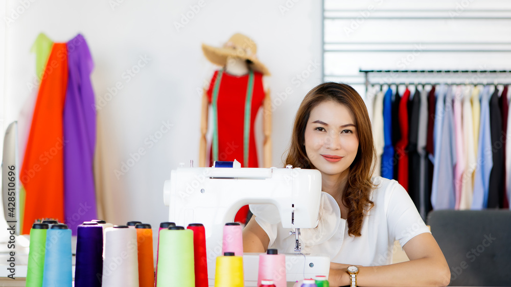 Asian young happy beautiful female seamstress sit smile use sewing ...