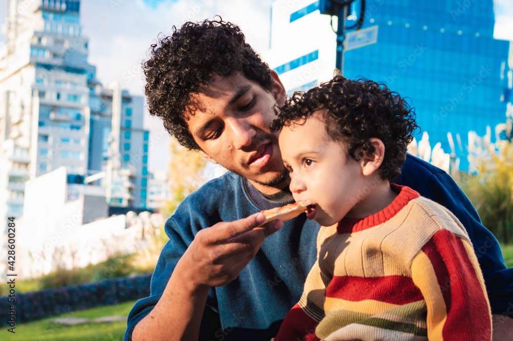 young black-skinned father, with his son in a square eating pizza ...