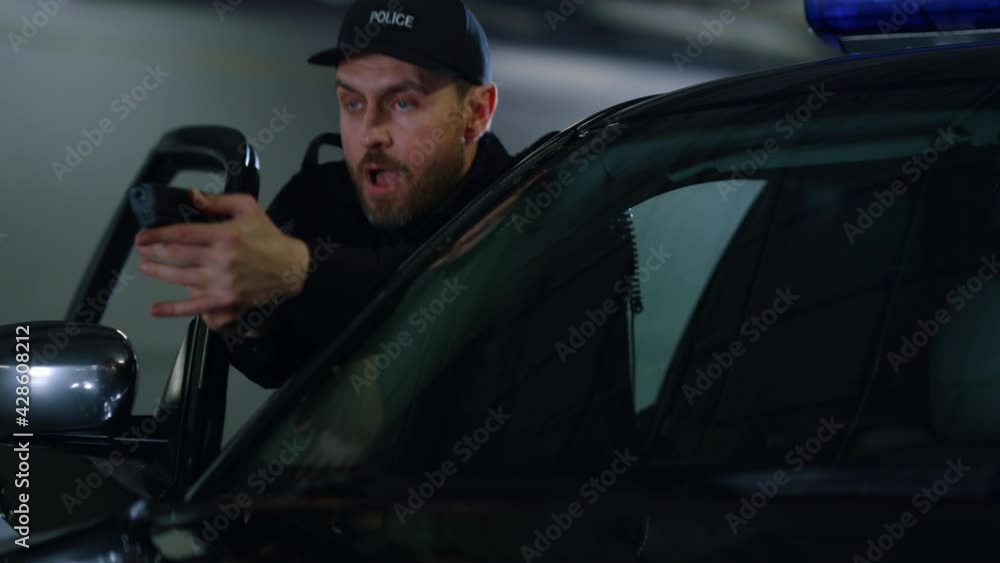 Policeman standing behind doors of police car. Cop aiming gun at police ...