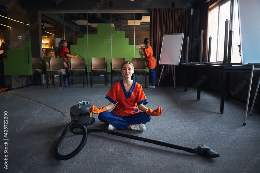 Calm cleaning lady in rubber gloves meditating after the vacuuming ...
