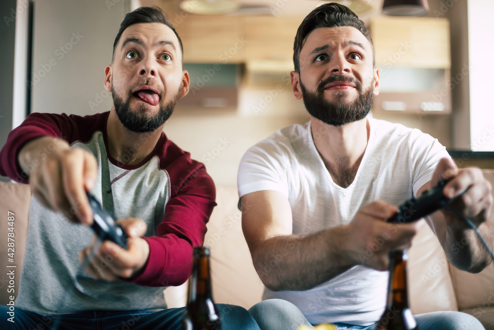 Excited smiling men playing in video games on tv at home on the couch ...
