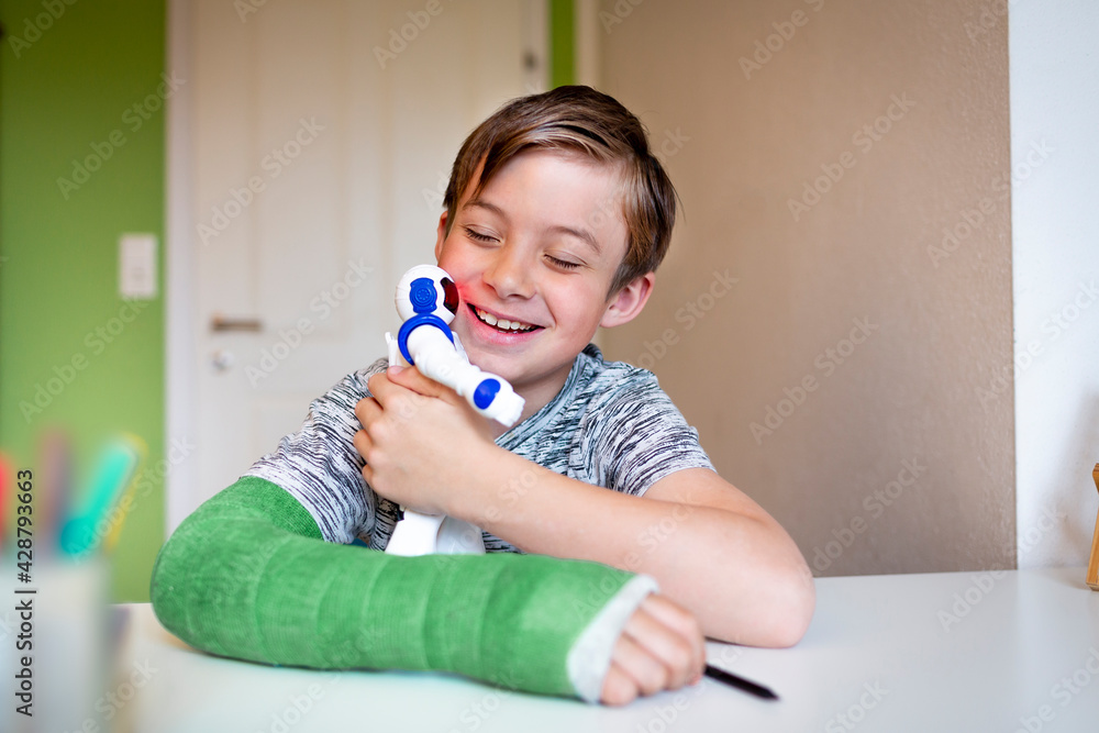 cool boy with green arm cast is sitting in his room and is playing with ...