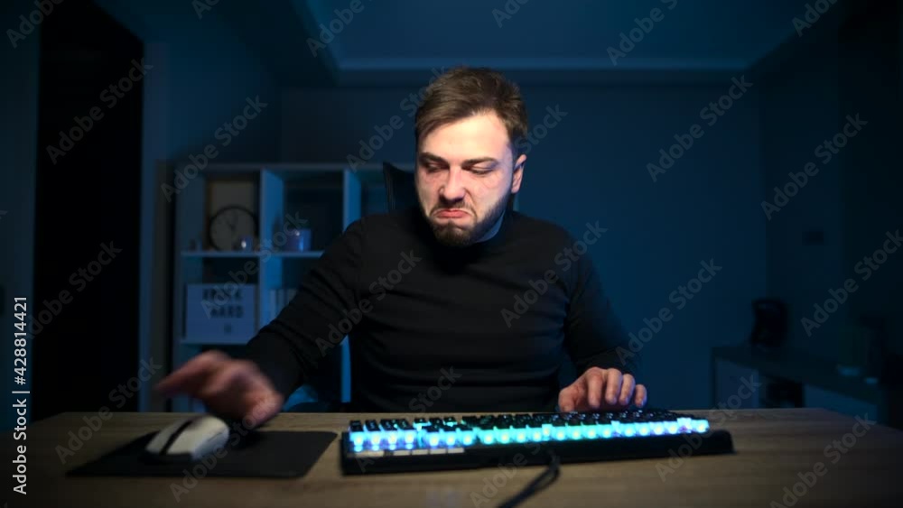 Сrazy bearded man gets angry at night at his computer desk, looks at ...