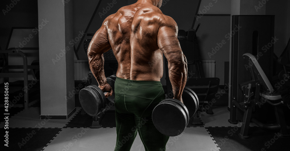 Powerful bodybuilder posing in the gym with dumbbells. No name portrait ...