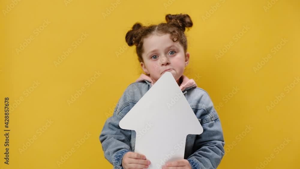 Hesitant small girl kid hold white arrow points sideways at upper right ...