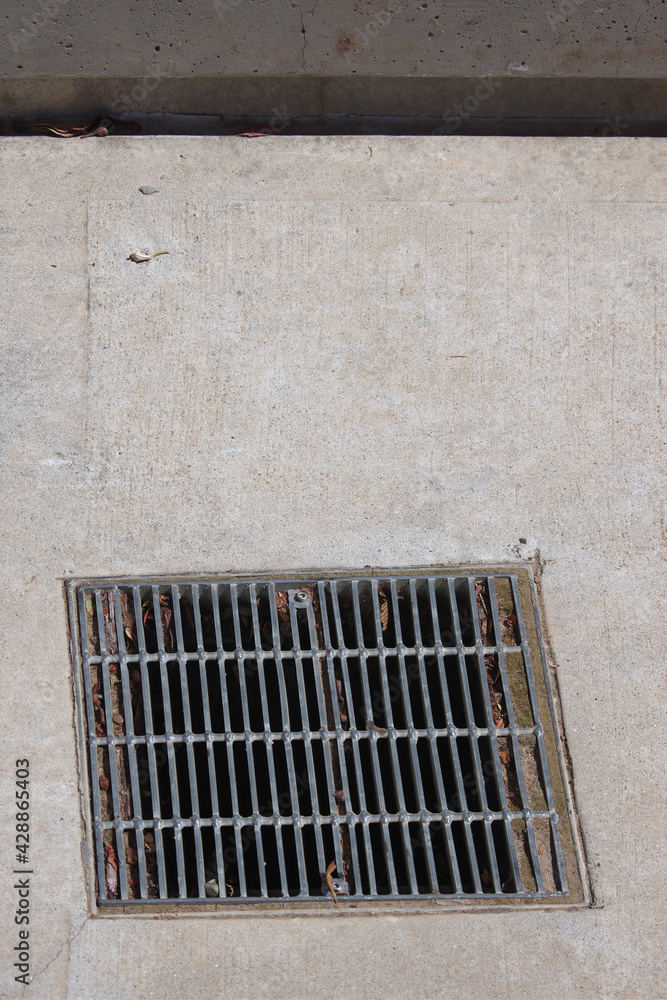 Iron grid cover of a drainage gully in concrete pavement with brown ...