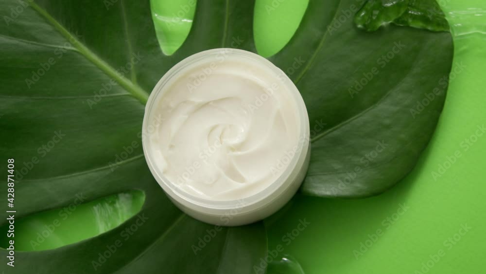 Cosmetic jar with cream on green tropical leaf in clean water splash on ...