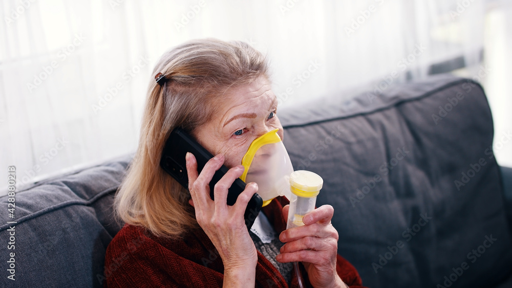 Elderly woman using oxygen inhaler while speaking on the phone ...