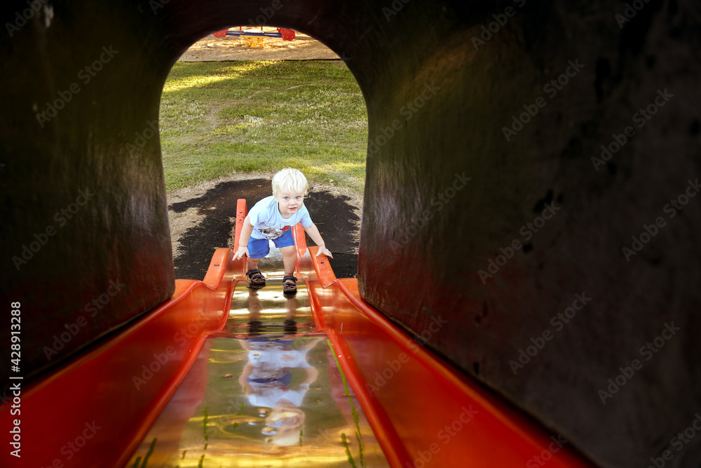 Little boy playing on vibrant red slide climbing up the wrong way Stock ...