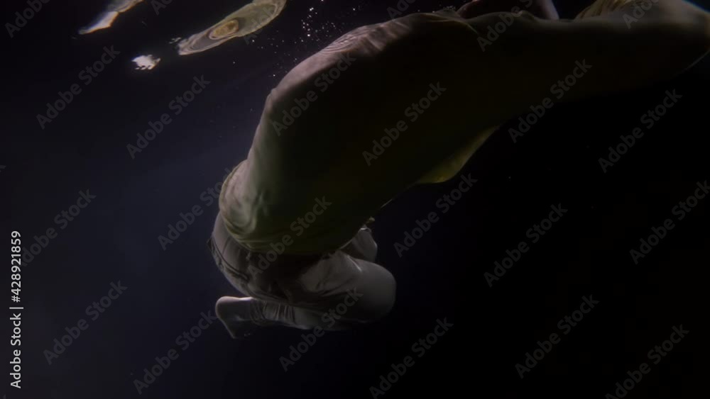 dressed man is floating underwater, sinking and diving in dark depth of ...