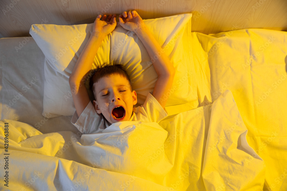 Cute little caucasian boy wake up in his comfortable bed in the morning ...