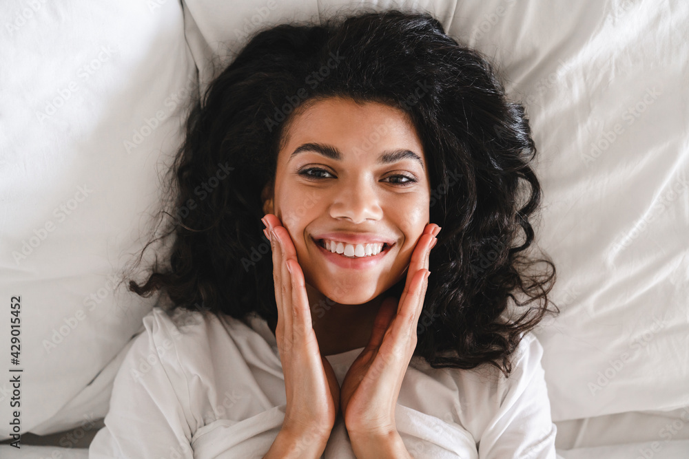 Close up portrait of a cheerful afro girl lying in her white bed in the ...