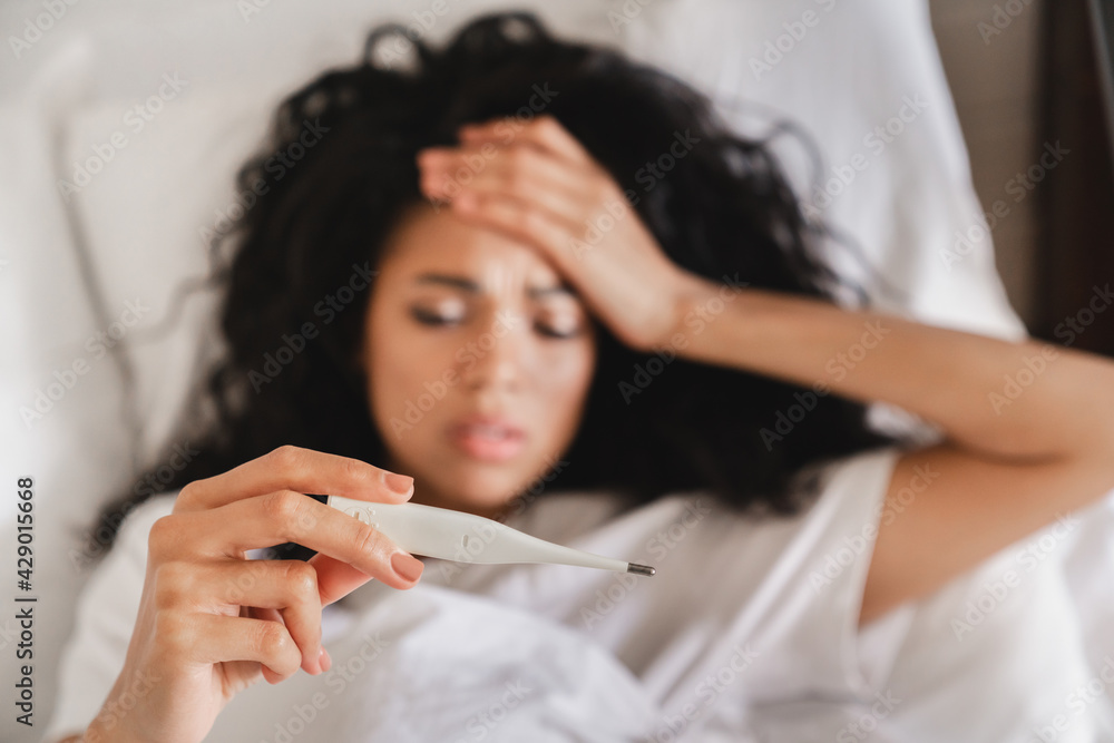 Ill sick young afro woman lying in bed with high fever looking at the ...