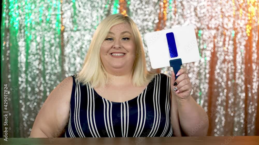 An enthusiastic blonde woman shows a number "1" number palette and ...