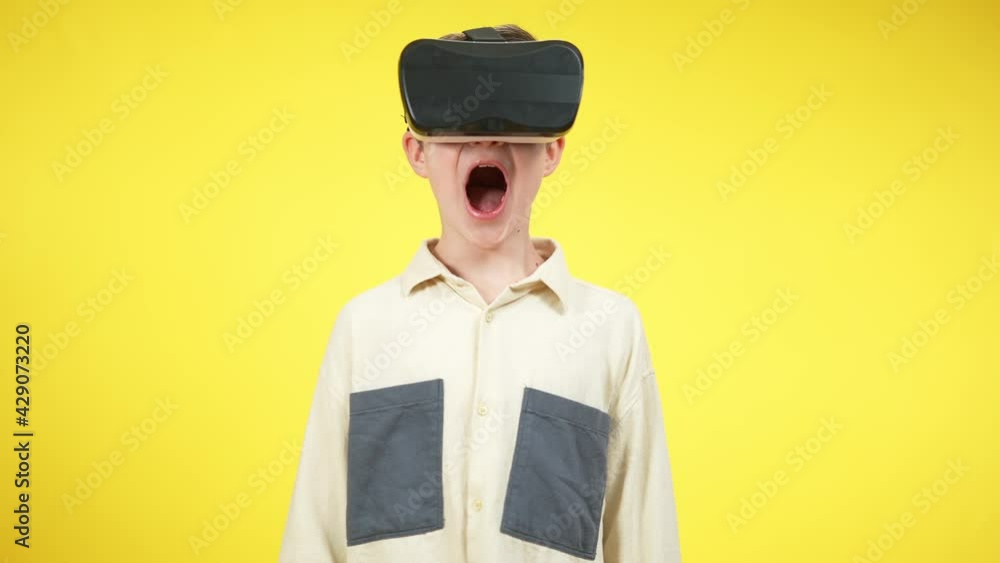 Caucasian boy in VR headset screaming at yellow background. Middle shot ...