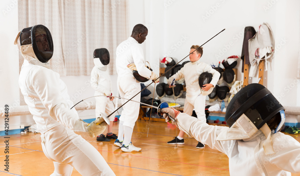 Adults and teens wearing a fencing uniform practicing with foil in a ...