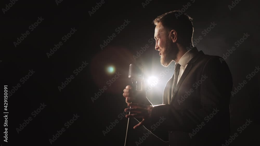 A man is standing on the stage and singing. He's holding a retro ...
