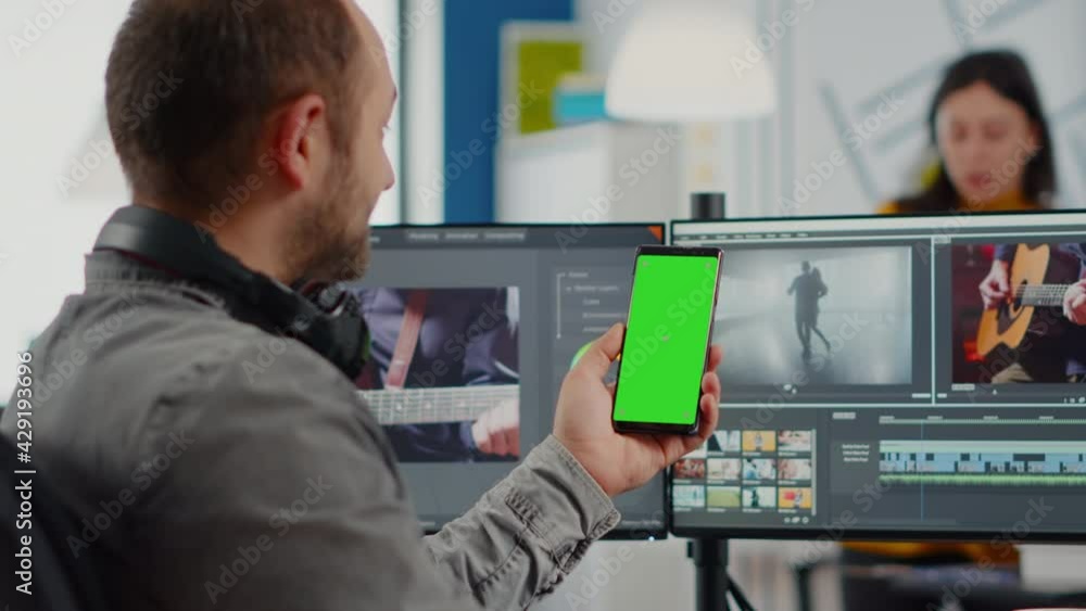 Video editor talking on video call holding smartphone with green screen ...