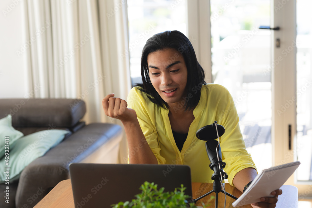 Mixed race transgender woman making podcast using microphone and laptop ...