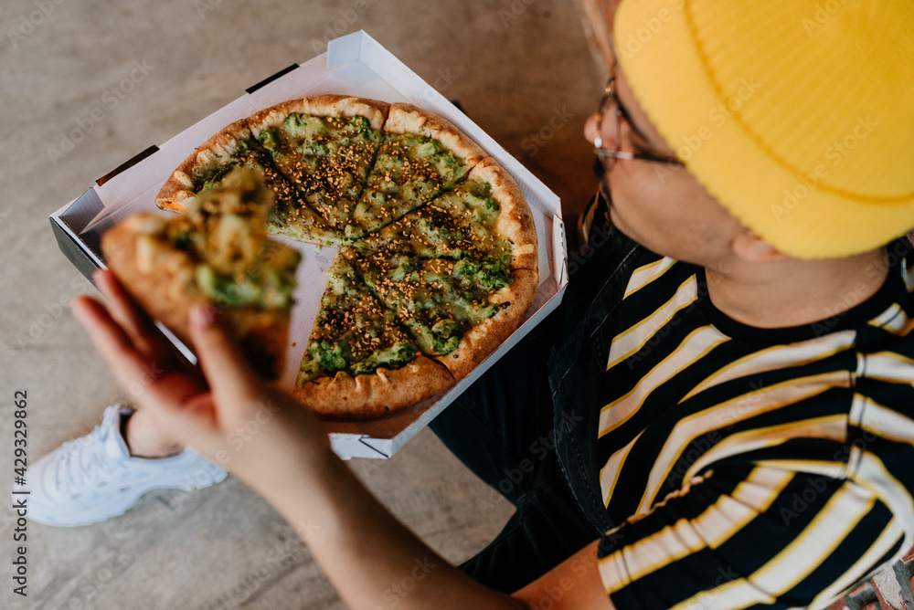 male model sitting on the floor eating a piece of pizza with his hand ...