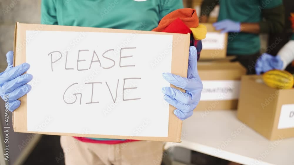 Volunteer holding donation box turning with please give signage message ...