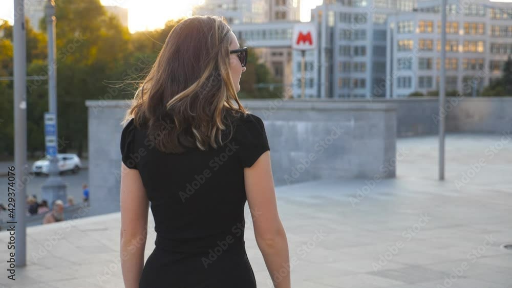 Young unrecognizable girl in black dress walking along urban street ...