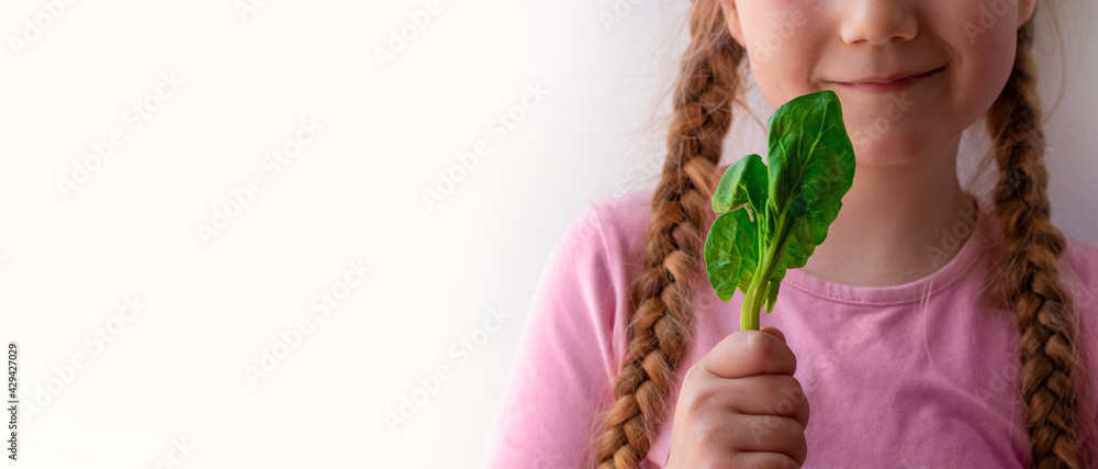 Little girl with fresh spinach in hand white background. Child eats ...