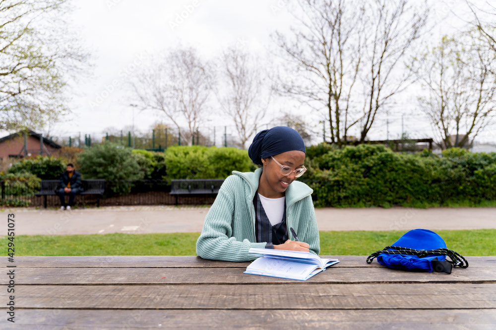 Black Muslim woman in park writing Stock Photo | Adobe Stock