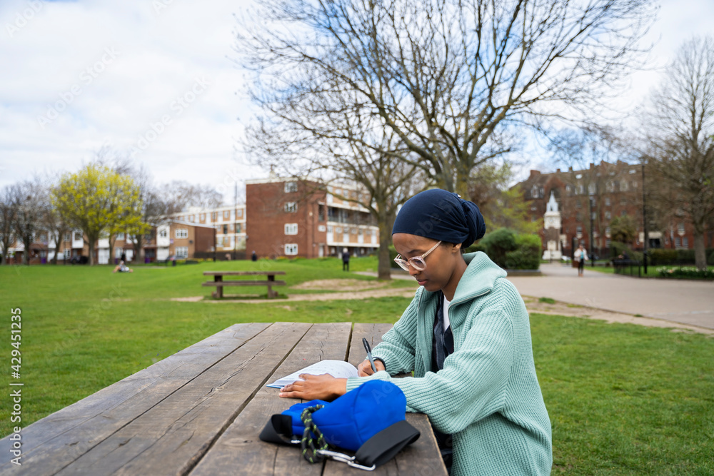 Black Muslim woman in park writing Stock Photo | Adobe Stock